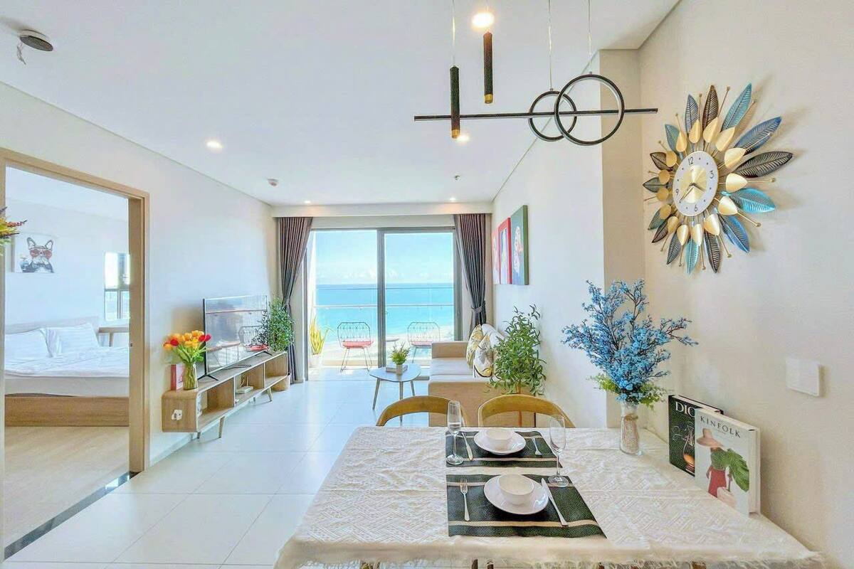 Quarto de hotel moderno com varanda, área de refeições e um relógio de parede decorativo.