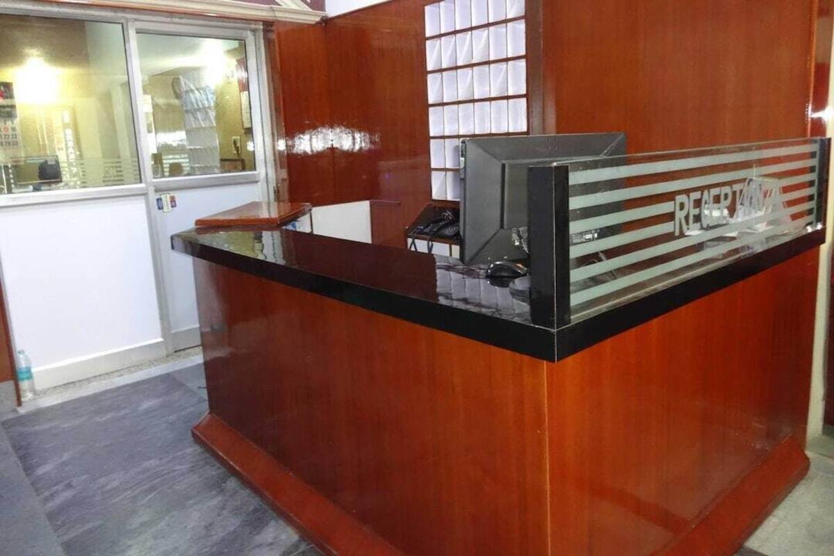 Balcão de recepção com acabamento em madeira, divisória de vidro e monitor de computador.
