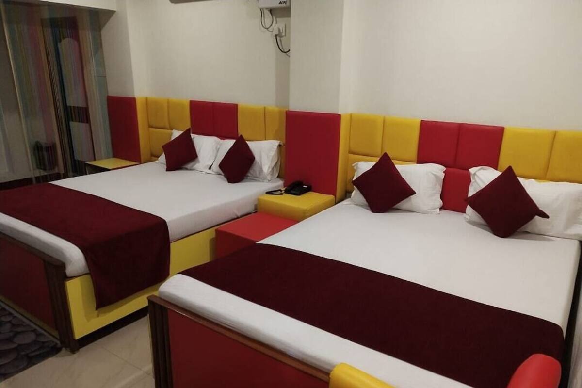 Quarto de hotel com duas camas, cada uma com cabeceira vermelha e amarela, roupa de cama branca e almofadas vermelhas.