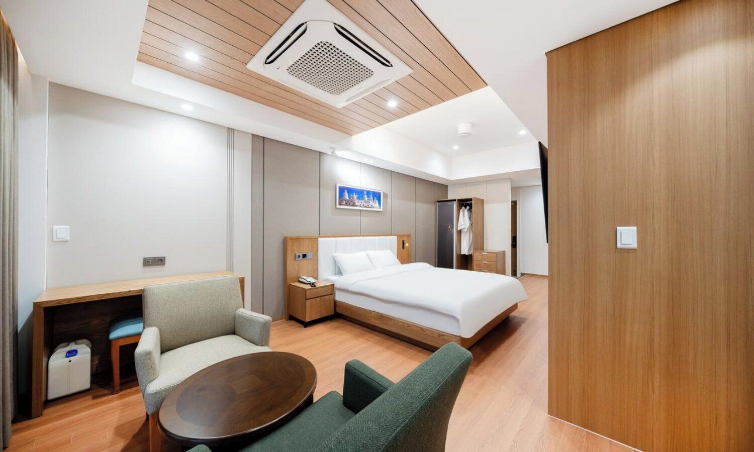 Quarto de hotel moderno com uma cama, escrivaninha, cadeira, mesa pequena e um guarda-roupa.