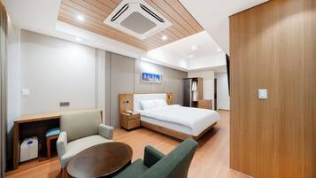 Quarto de hotel moderno com uma cama, escrivaninha, cadeira, mesa pequena e um guarda-roupa.
