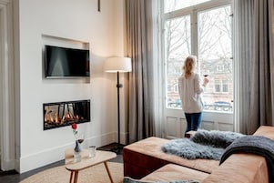 Uma sala de estar moderna com lareira, televisão de tela plana e uma grande janela com vista para a cidade.