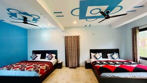 Quarto de hotel com duas camas, um ventilador de teto, uma janela grande com cortinas e um piso estampado.