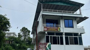 Um edifício de dois andares com uma placa indicando 'Green Valley Hotel & Restaurant', com informações sobre café da manhã, almoço, jantar e quartos.