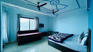 Quarto com cama, um banco, ventilador de teto, televisão e janela.