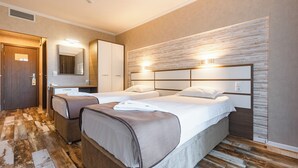Quarto de hotel com duas camas, um espelho grande, um guarda-roupa e piso de madeira.