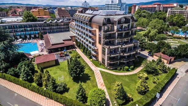 Um hotel de vários andares com piscina, rodeado por vegetação e outros edifícios.