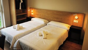 Quarto de hotel com duas camas, cabeceira de madeira, luminárias de cabeceira, guarda-roupa e uma janela.