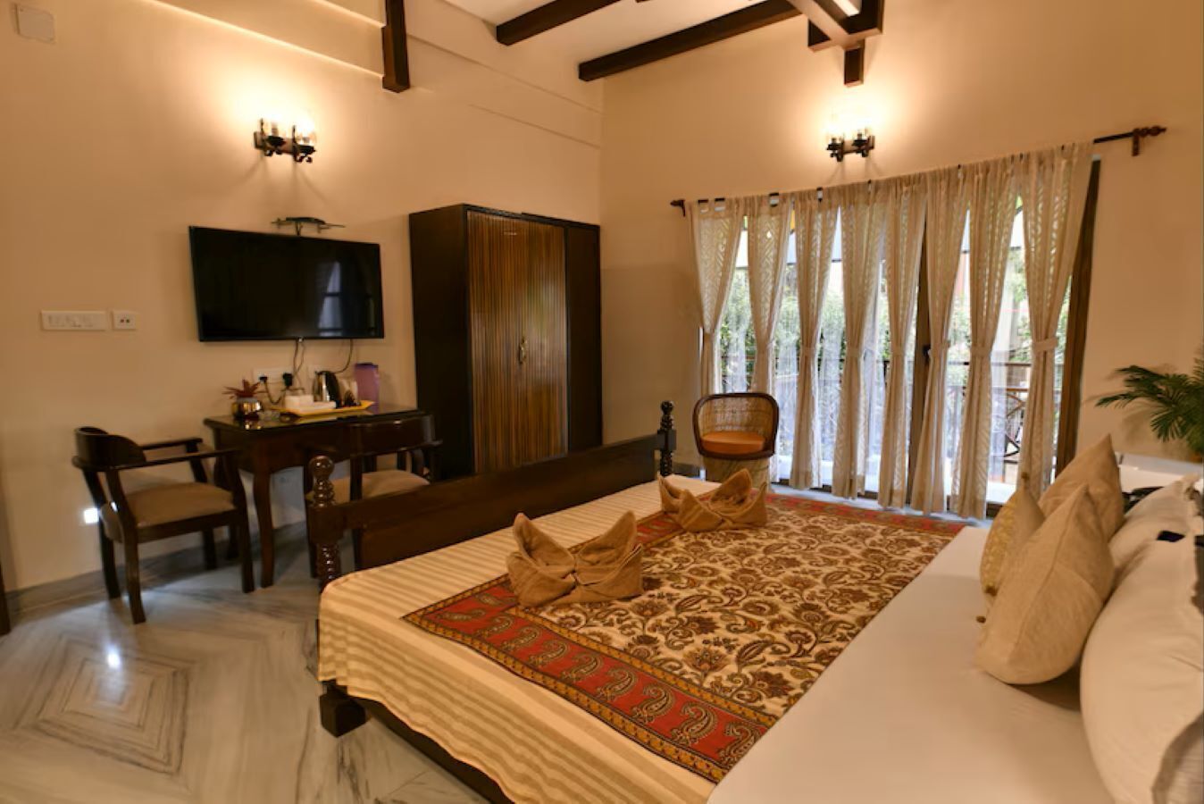 Quarto de hotel com cama, escrivaninha, cadeira, televisão e janela com cortinas.