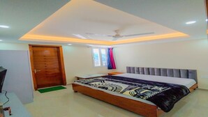 Um quarto com cama, ventilador de teto, janela com cortinas e uma porta.