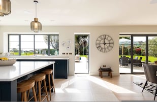 Uma cozinha moderna com uma ilha grande, banquetas, um relógio e vista para o exterior.