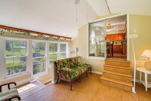 Um quarto amplo com janelas grandes, escada de madeira, sofá de vime e vista para o exterior.