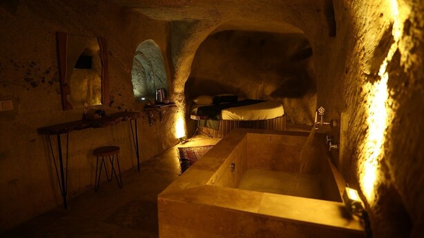 Interior que lembra uma gruta, com uma banheira, uma pequena mesa e um espelho.