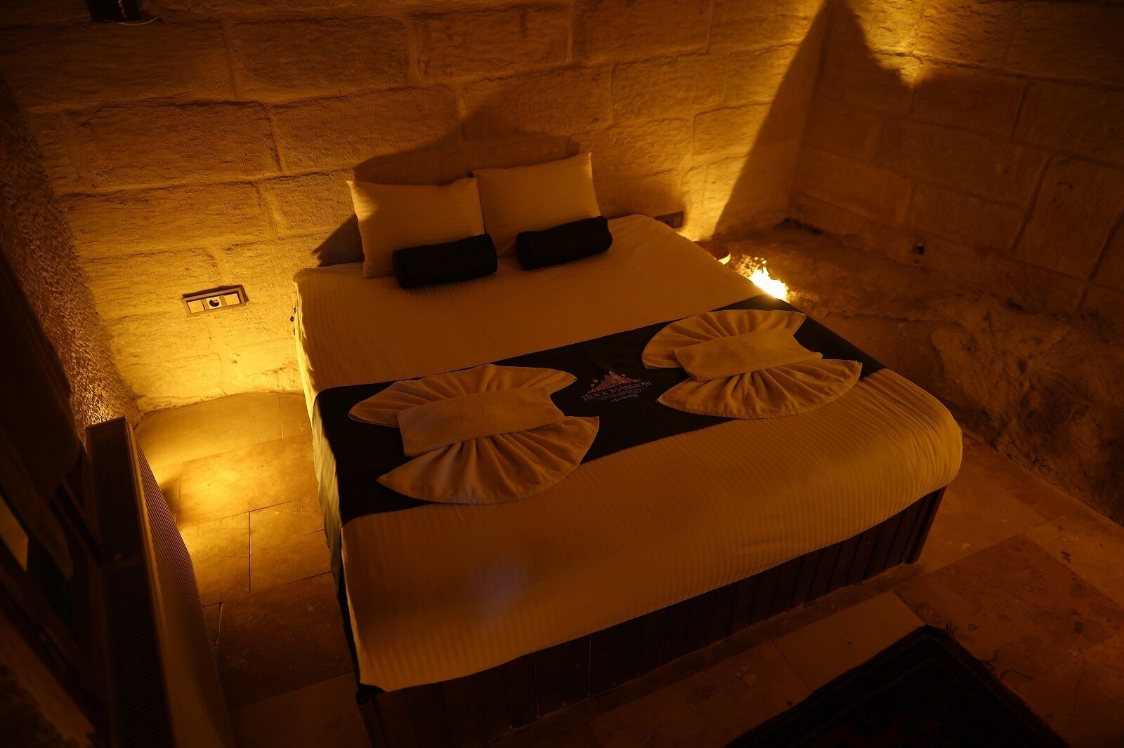 Cama com travesseiros e cobertor em quarto com paredes de pedra.