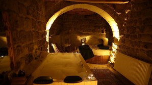 Quarto com paredes de pedra, banheira de madeira, um banco de madeira e um radiador.