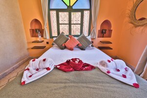 Quarto de hotel com cama, almofadas, uma garrafa e toalhas.