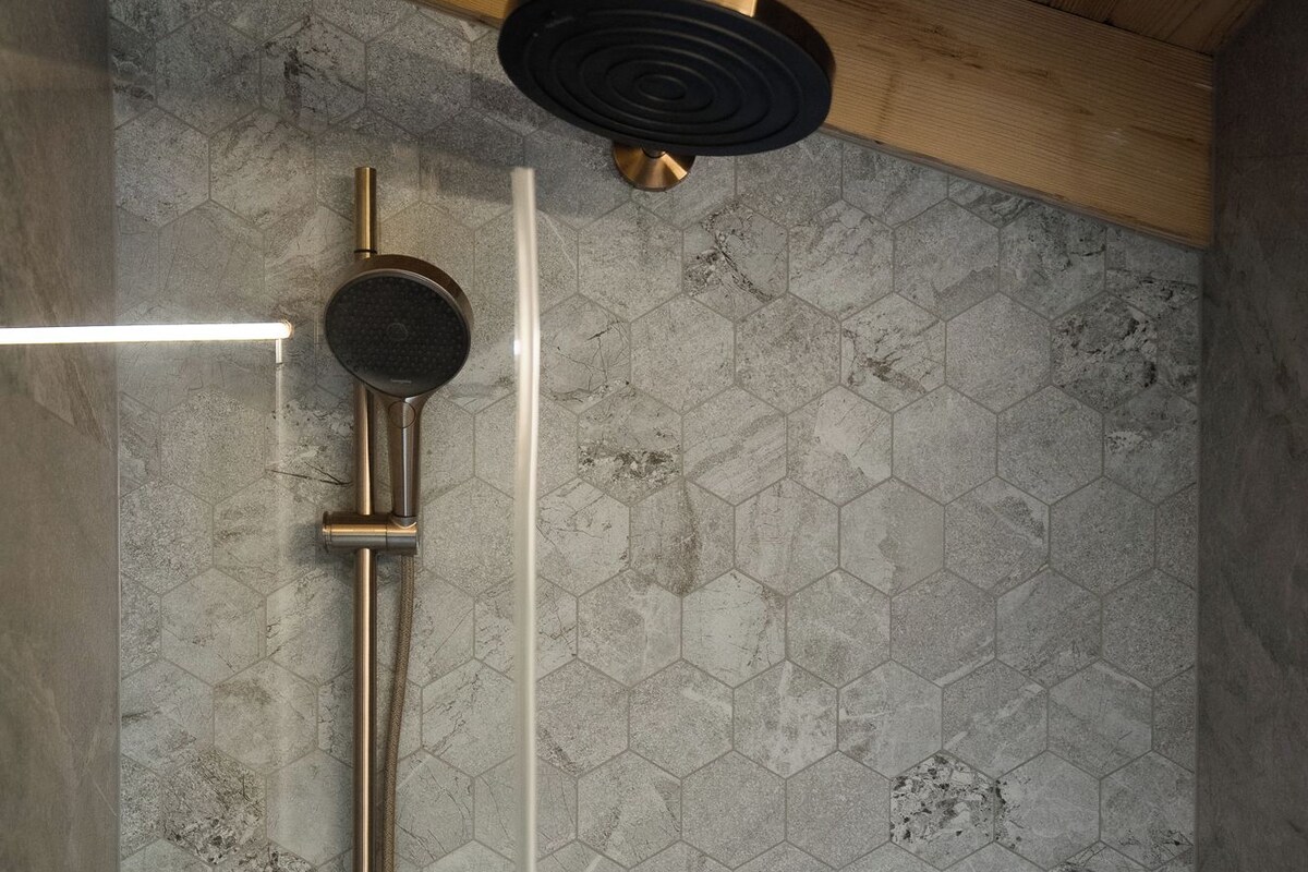 Chuveiro com box de vidro, chuveiro manual e painel de controle fixado na parede.