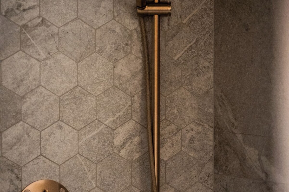 Chuveiro com padrão de azulejos hexagonais na parede e torneira de latão.
