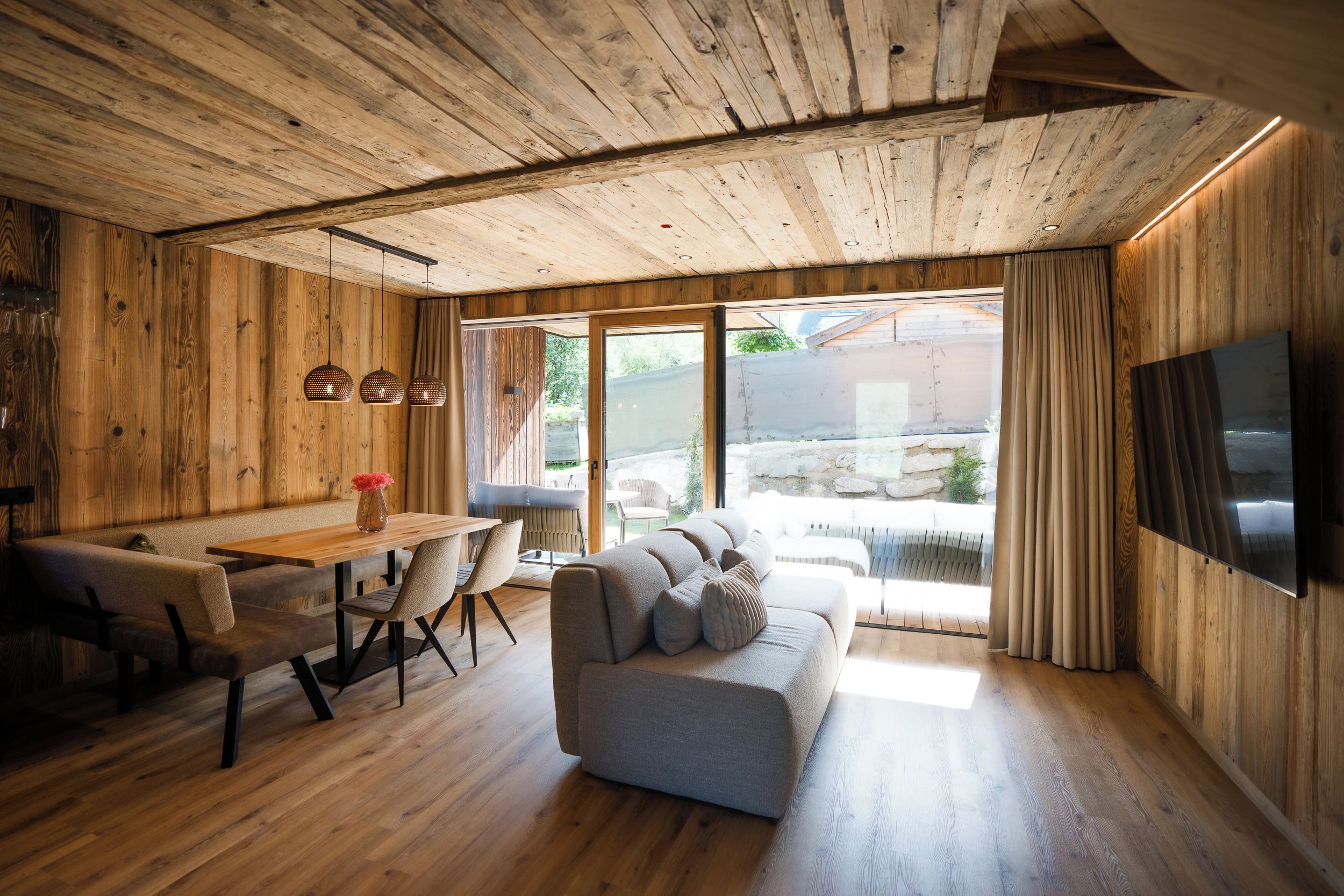Interior moderno com paredes de madeira, área de refeições, sofá e televisão.