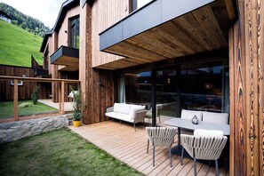Uma casa moderna de madeira com um espaço de varanda equipado com sofá, cadeiras e mesa.