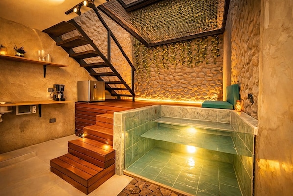 Um interior moderno com parede de pedra, escada de madeira, banheira de hidromassagem com azulejos verdes e uma máquina de café.