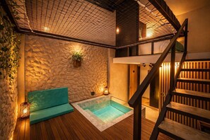 Uma área de spa com parede de pedra, um banco de madeira, uma piscina pequena e uma escadaria.