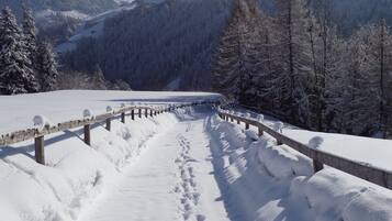 Uma trilha coberta de neve com grades de madeira, serpenteando por uma paisagem montanhosa com árvores perenes e picos distantes.