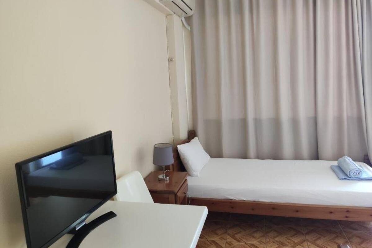 Quarto de hotel com cama, televisão, luminária e ar condicionado.