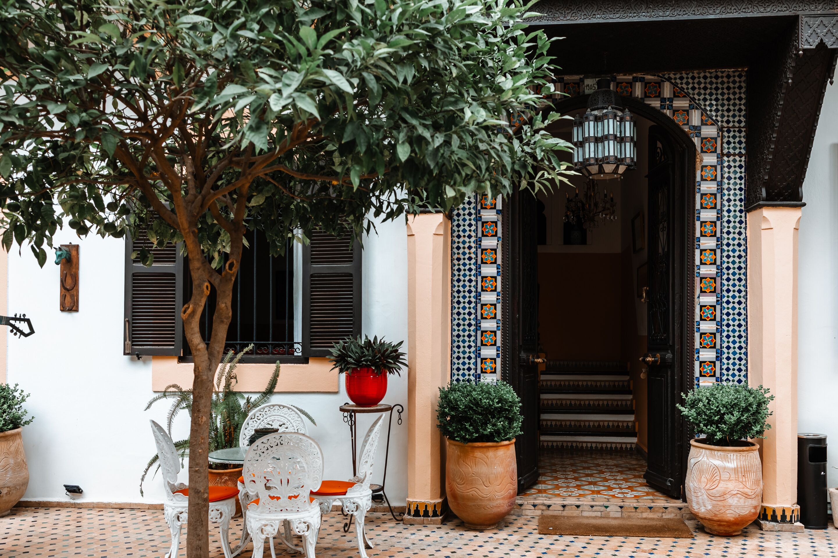 Entrada de um edifício com chão de azulejos, uma árvore e plantas em vasos.