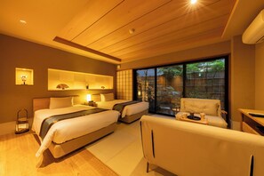 Quarto com duas camas, um sofá, uma mesinha e uma janela grande com vista para áreas verdes.