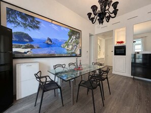 Uma cozinha moderna com uma ilha grande, uma área de jantar com mesa de vidro e uma televisão grande exibindo uma vista panorâmica.