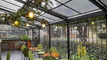 Uma área de estar coberta ao ar livre, com mesas e cadeiras, rodeada por vegetação e vista para o exterior.