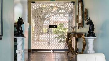 Um corredor com um candelabro, uma cadeira branca, uma mesa com uma estátua de cavalo e um portão decorativo.