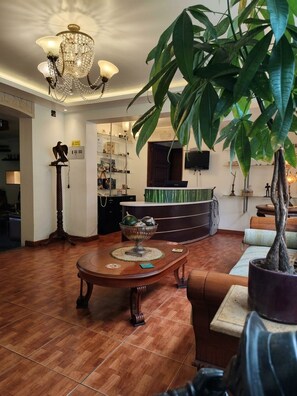 Ampla sala de estar com lustre, mesa de centro redonda de madeira, sofá e uma grande planta em vaso.