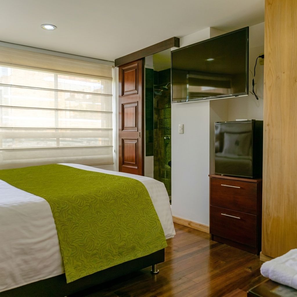 Quarto de hotel com cama, televisão, guarda-roupa de madeira e janela com persianas.
