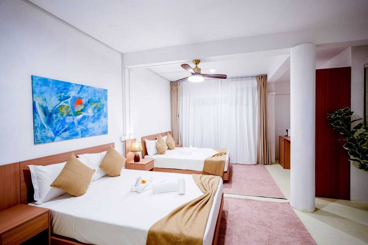 Quarto de hotel com duas camas, um ventilador de teto, um quadro e uma planta.