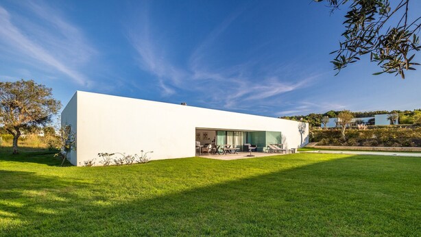 Uma casa moderna com telhado plano, janelas amplas e área de pátio.