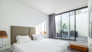 Quarto de hotel moderno com uma cama grande, uma mesinha, um abajur e uma janela ampla com vista.