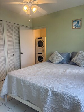Quarto com cama, ventilador de teto, máquina de lavar e porta com venezianas.