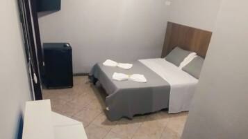 Quarto de hotel pequeno com uma cama, mesa de cabeceira, cadeira, televisão e lixeira.