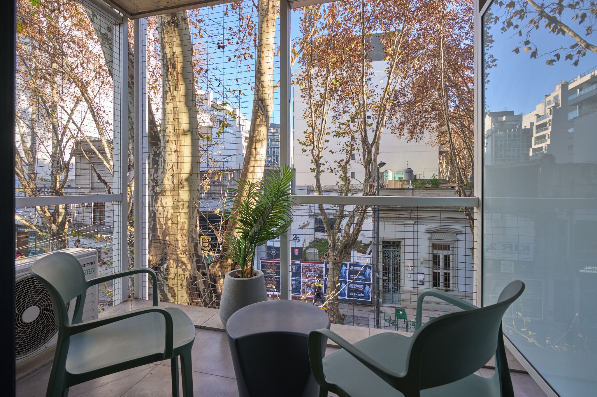 Varanda com cadeiras, um vaso de planta e vista para árvores e edifícios.