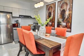 Cozinha moderna com área de refeições, cadeiras laranja, mesa de madeira e um vaso com flores.
