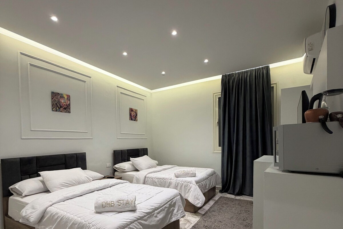 Quarto de hotel moderno com uma cama grande, duas camas menores, uma TV de tela plana e ar condicionado instalado.