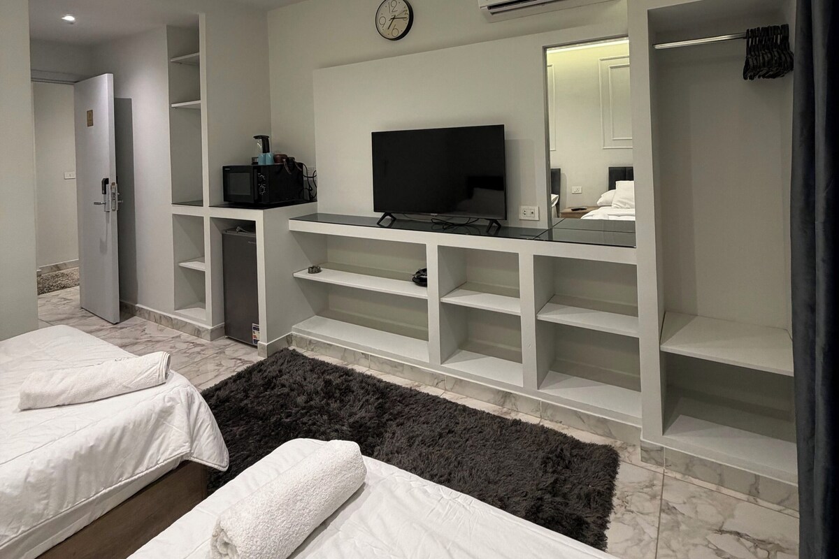 Quarto de hotel com duas camas, uma televisão, um relógio e um aparelho de ar condicionado.