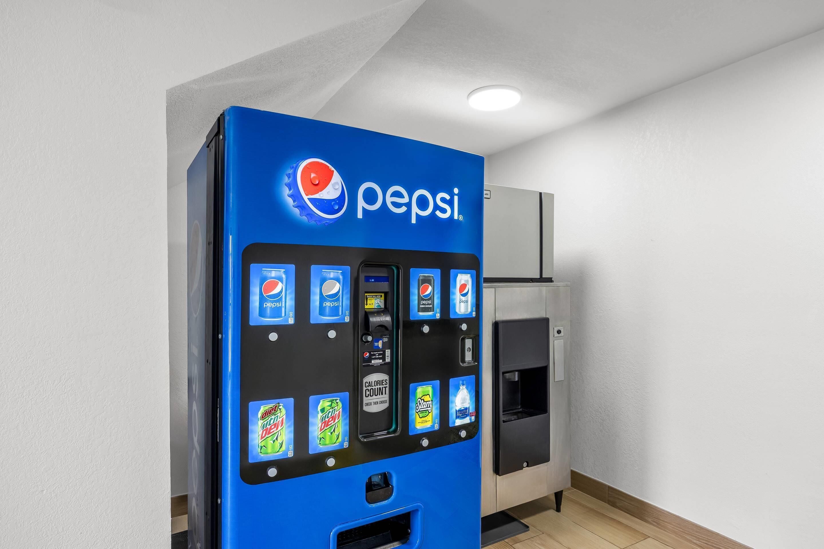Máquina automática azul da Pepsi com um dispensador de água e um micro-ondas ao fundo.