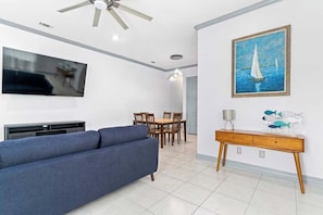 Uma sala de estar moderna com sofá, televisão, área de refeições e um quadro de um veleiro.
