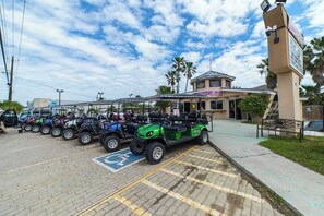 Um estacionamento com vários carrinhos de golfe e um edifício com uma placa que diz 'RESORT TICKETS'.