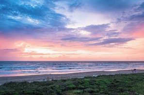 Uma praia com pôr do sol, ondas do oceano e uma pessoa caminhando.