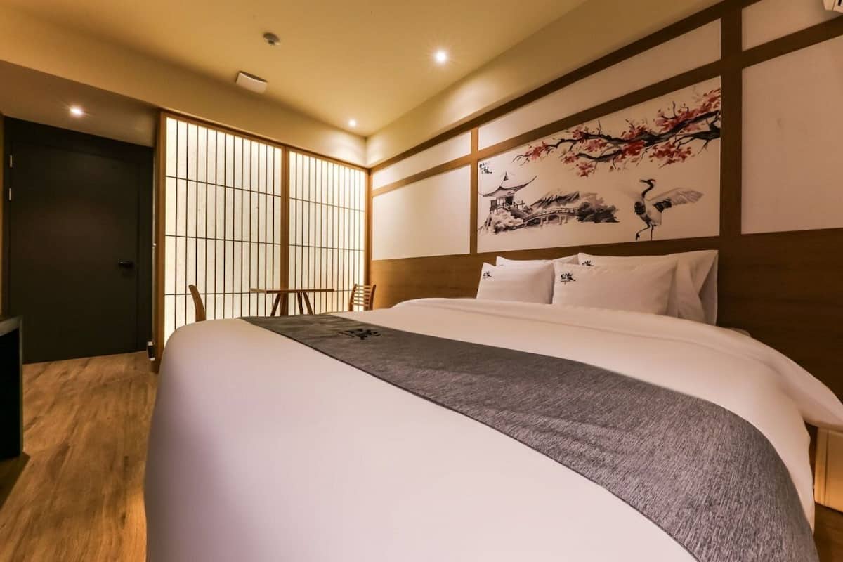 Quarto de hotel com uma cama grande, cabeceira de madeira, um separador japonês e um quadro na parede.