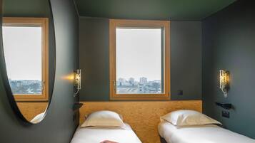 Quarto de hotel com duas camas, janelas amplas e luminárias fixadas na parede.